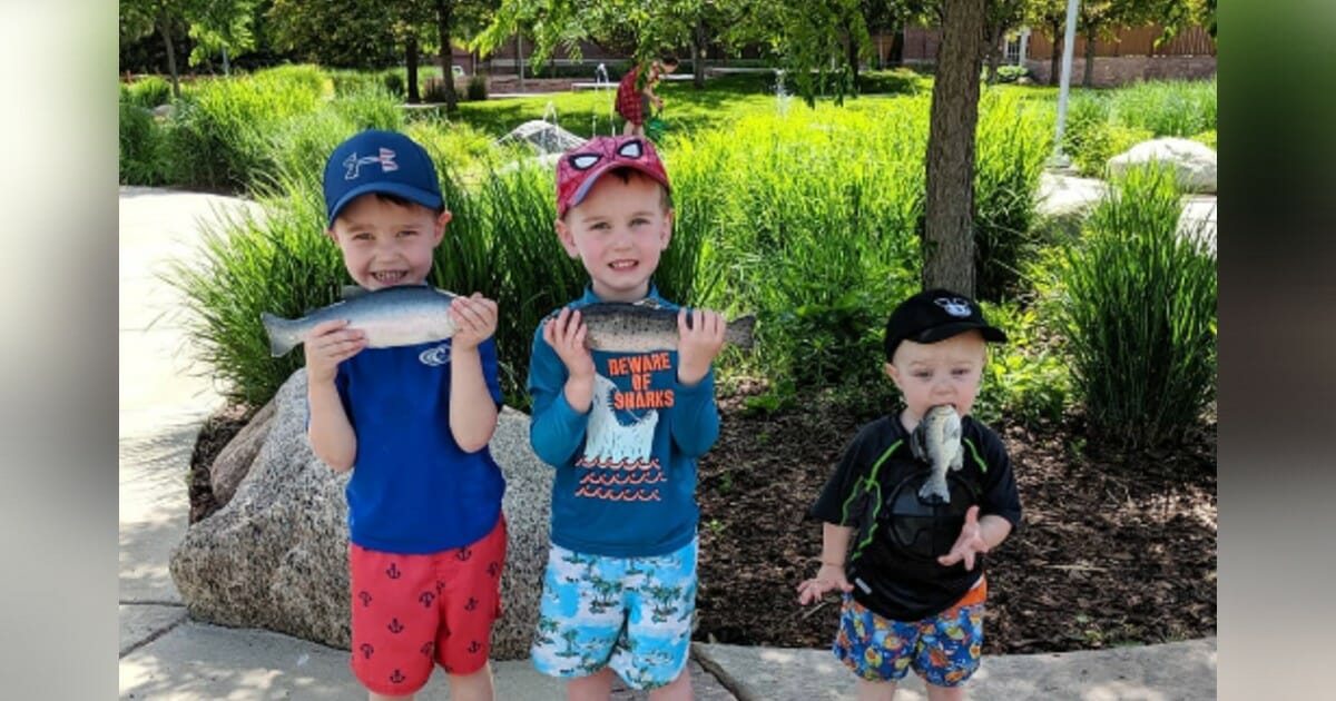 Toddler shoves rubber fish in mouth while brothers pose for family photo