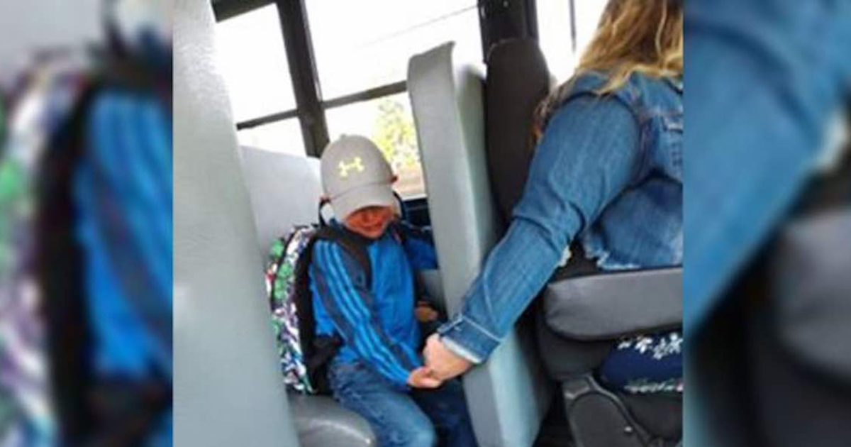 Bus driver holds hand of crying boy on his first day of school